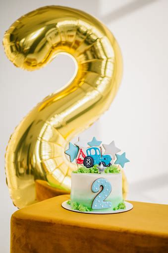 젤 풍선의 배경에 2 살짜리 케이크 그림 트랙터와 별이 있는 케이크는 소년을 위한 녹색 파란색 장식으로 장식되어 있습니다 생일 축하 파티에서 맛있는 리셉션 축제 디저트의