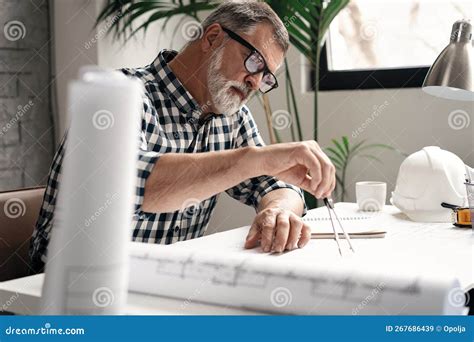 Mature Architect Working On Construction Blueprint In Modern Office