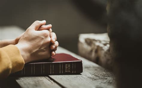 그리스도인의 삶의 위기를 하나님께 드리는 기도 손을 잡은 여자는 나무 식탁에서 더 나은 삶을 살기를 바라는 하나님의 축복을 간구합니다 여자는 성경으로 하나님께 기도하는 손을