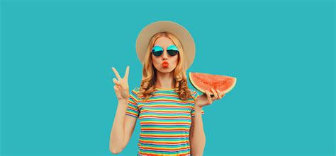 신선한 육즙이 많은 수박 조각이 입술을 날리는 아름다운 젊은 여성의 여름 초상화는 파란색 배경에 밀짚모자를 쓰고 공기 키스를 보낸다 25 29세에 대한 스톡 사진 및 기타