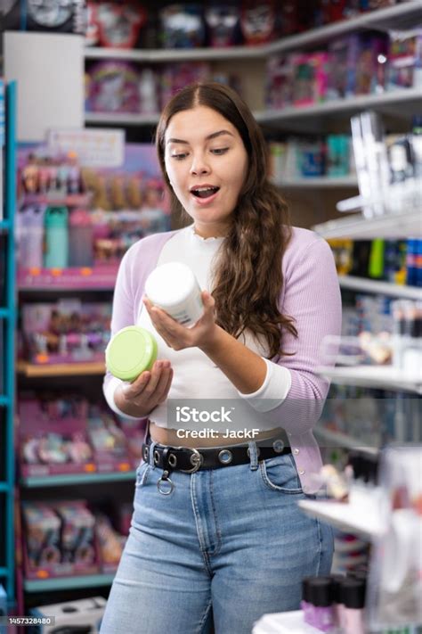 긍정적 인 매력적인 여자는 미용 가게에서 쇼핑하는 동안 두 개의 크림을 들고 비교 20 24세에 대한 스톡 사진 및 기타 이미지 20 24세 각질제거 갈색 머리