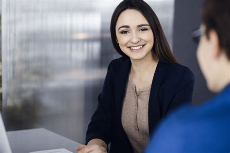 젊은 아름다운 사업가가 현대 사무실의 책상에 앉아있는 동안 동료와 이야기하고 있습니다 비즈니스 성공의 개념 20 24세에 대한 스톡 사진 및 기타 이미지 Istock
