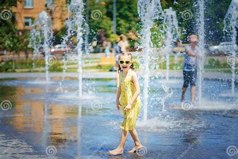 Девушка в желтом платье играя и имея потеху наслаждаясь брызгами фонтана Стоковое Фото