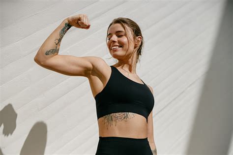 웃는 여자 운동 선수 팔을 올리고 현대 건물 배경에 서있는 동안 팔뚝을 보여줍니다 운동에 대한 스톡 사진 및 기타 이미지 운동 힘 건강한 생활방식 Istock