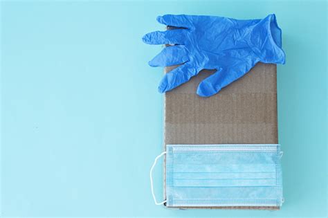 파란색 라텍스 장갑과 의료 용 마스크의 상단 보기는 밝은 파란색 배경에 골판지 상자 소포에 거짓말 텍스트 공간 안전한 배달 개념