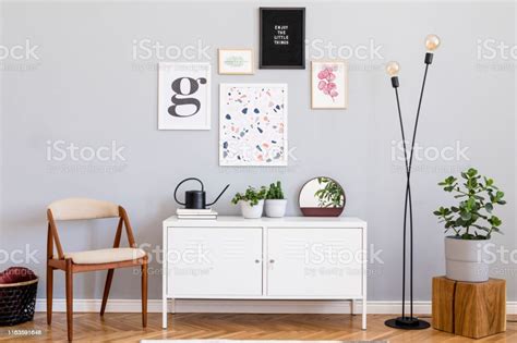 포스터 갤러리 벽 흰색 선반 의자 식물 램프 및 우아한 액세서리를 모의 로 열린 공간의 스칸디나비아 홈 인테리어를 디자인합니다 회색 배경 벽입니다 복고풍의 아늑한 홈 장식