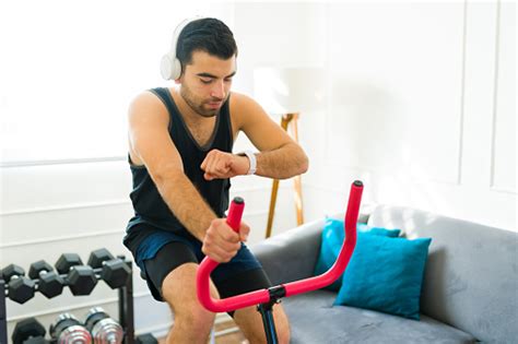 고정식 자전거를 타는 동안 스마트워치를 사용하는 피트니스 남자 20 29세에 대한 스톡 사진 및 기타 이미지 20 29세 거실 건강한 생활방식 Istock