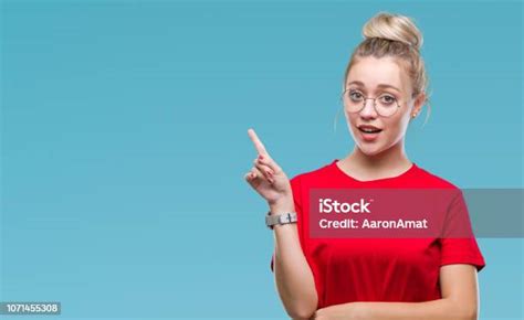 젊은 금발 여자 얼굴에 큰 미소와 함께 고립 된 배경 위에 안경을 쓰고 카메라를 보고 옆에 손 및 손가락으로 가리키는 금발 머리에 대한 스톡 사진 및 기타 이미지 Istock