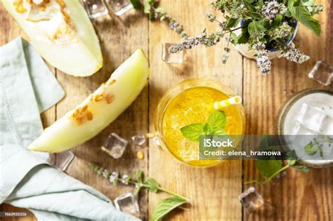 상쾌한 과일 향이 나는 여름 음료 계절 음료 멜론 레모네이드가 나무로 된 소박한 테이블에 얼음과 민트를 곁들인 잔에 담겨 있다