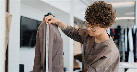 젊은 갈색 머리 곱슬 여자는 그녀의 스튜디오에서 일하는 동안 마네킹에 재킷의 소매 길이를 측정 사진 Unsplash의 청녀 이미지