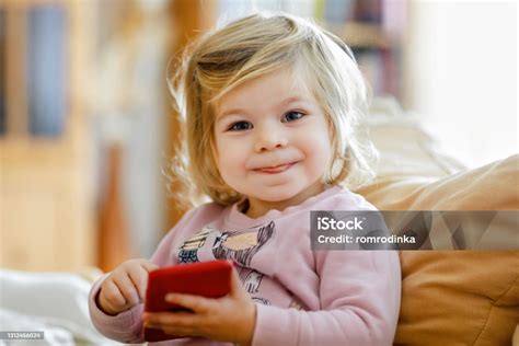 집에서 스마트 폰으로 노는 귀여운 어린 유아 소녀 건강한 아기손가락으로 전화를 건드리고 만화를 찾고 교육 용 게임을 재미있게 즐길 수 있습니다 조기 개발 개념 가정 생활에