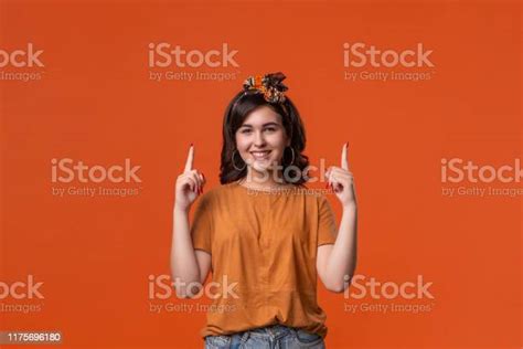 예쁜 갈색 머리 여자 에 티셔츠와 아름 다운 머리띠 가리키는 그녀의 손가락으로 오렌지 배경 위에 고립 된 광고를 위한 장소입니다