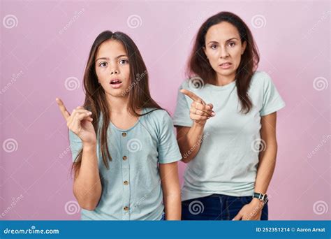 Young Mother And Daughter Standing Over Pink Background Pointing Aside