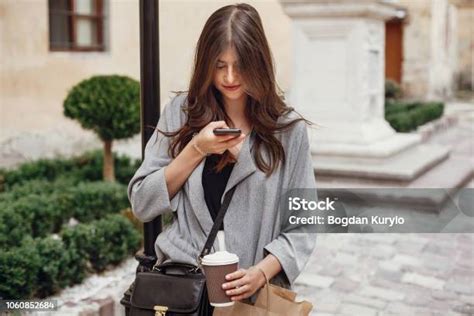 아름 다운 머리 들고 전화 커피 컵 봉투 그리고 피트의 복용 사진 도시에서 거리를 가진 유행 Hipster 소녀 화려한 행복 한 젊은 여자의 시간을 즐기고 하 고 소셜