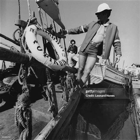 Male Model Posing On A Boat In The Harbor Of Aegina In Greece Wearing