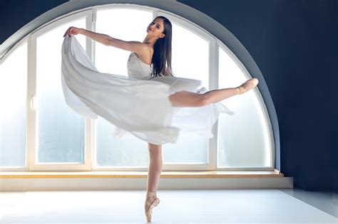 하얀 투투 의상을 입은 젊은 발레리나 자연스러운 주변 일광 분위기 속에서 큰 둥근 모양의 창 배경 앞 발레 스튜디오에서 발레 스튜디오로 이동 20 24세에 대한 스톡 사진
