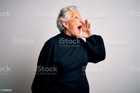 캐주얼 한 검은 스웨터를 입고 고립 된 흰색 배경 위에 서있는 선임 아름다운 여성은 입에 손을 대고 큰 소리로 외치고 비명을 지르고 있습니다 통신 개념입니다 노인에 대한