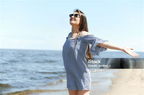 두 손을 벌리고 서 있는 바다 해변에서 자유로운 행복을 누리고 있는 행복한 미소 짓는 여자 여름 드레스를 입은 갈색 머리 여성