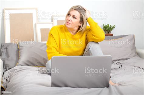 한 여성이 침대에 앉아 노트북을 들고 창밖으로 나와 전략을 고민하고 있다 문제를 해결합니다 집에서 일 프리랜서 색상 트렌드 2021 시간에 대한 스톡 사진 및 기타 이미지