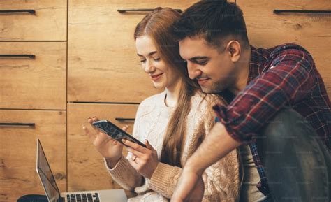 귀여운 백인 커플이 부엌 바닥에 앉아 휴대폰을 들고 미소를 지으며 노트북을 사용하고 있다 사진 Unsplash의 몰도바 이미지