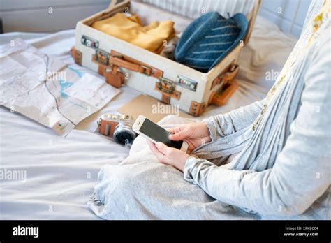 Woman Looking At Her Phone While Getting Ready For A Trip On The Bed