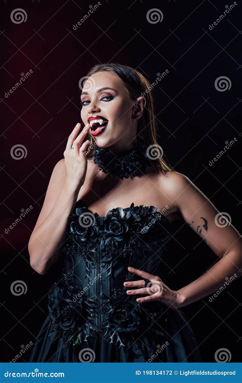 Vampire Girl With Fangs In Black Gothic Dress Isolated On Black Stock