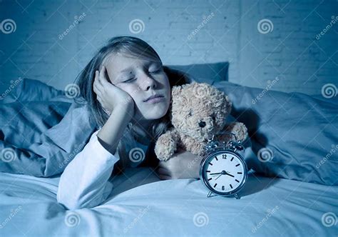 Маленькая девочка в кровати просыпается вечером зевать и чувствовать неусидчива показывающ часы