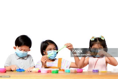 흰색 배경이있는 나무 테이블에 점토 장난감을 함께 연주하는 동안 얼굴 마스크를 착용 하는 아시아 어린이 아이들의 새로운 정상 아이들을위한 코로나 바이러스 보호 어린이의