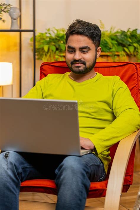 Young Man Freelancer Sitting On Chair Working On Laptop Pc Browsing Internet In Living Room At