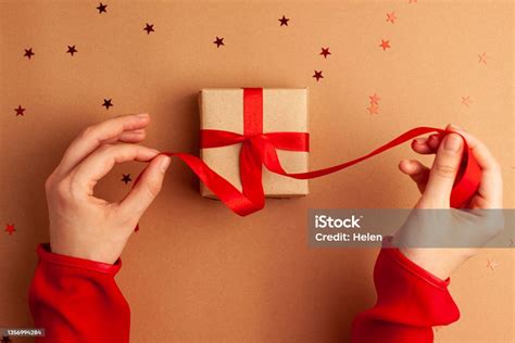 빨간 소매와 인간의 손은 빨간색 별 모양 크리스마스 휴일 개념 평면 누워 갈색 배경에 빨간 새틴 리본 활갈색 종이 선물을