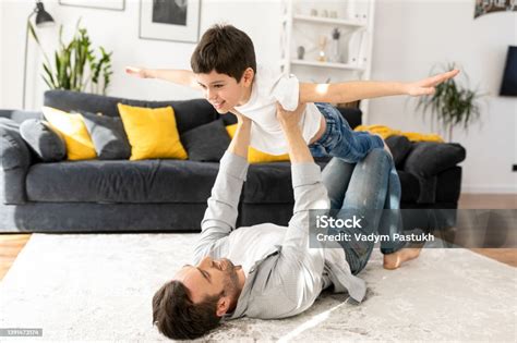 사랑스러운 아버지는 소니와 놀아요 행복한 아버지와 학령기 아들은 집에서 함께 시간을 보내고 아늑한 거실에서 바닥에 누워있는 재미를 소년을 안고있는 아빠 사진 이미지에 대한