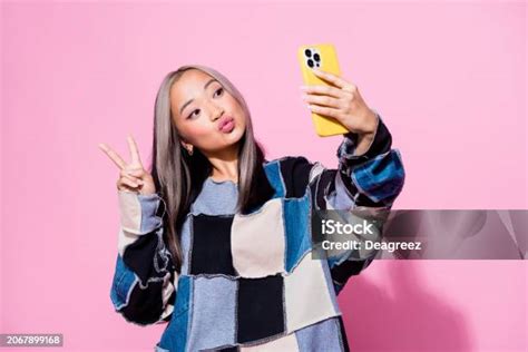 염색 한 머리를 한 매력적인 소녀의 사진 풀오버 스마트 폰에서 셀카를 찍는 것은 분홍색 배경에 고립 된 V 기호 삐죽 삐 셀카에