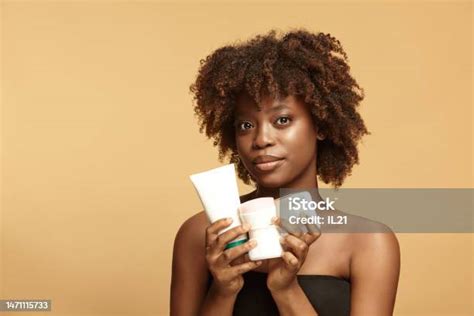 성인 아프리카계 미국인 민족 소녀는 베이지색 배경에 얼굴 근처에 다양한 크림 항아리를 거의 들고 있지 않습니다 깨끗한에 대한 스톡 사진 및 기타 이미지 Istock
