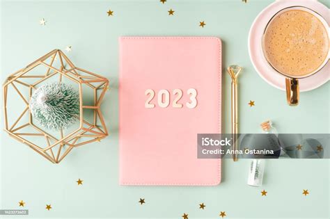 2023 글자 텍스트가있는 크리스마스 핑크 메모장 플랫은 플래너 커피 한 잔 양초 크리스마스 장식 노트북 및 문구류가있는 녹색 민트 테이블 배경에 누워 있습니다 상단보기