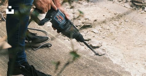 파란색 셔츠와 검은색 반바지를 입은 남자가 검은색과 파란색 전동 공구를 들고 있다 사진 Unsplash의 무료 의복 이미지