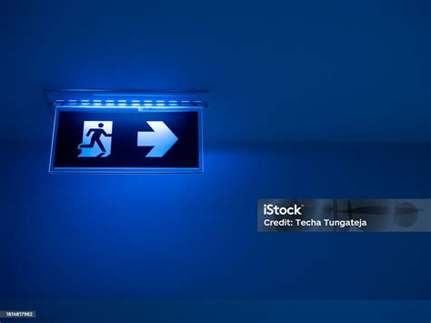 어두운 건물의 천장에 Led 조명 화재 탈출 표지판의 파란색 톤이 걸려 있습니다 비상 화재 출구 표지판 실행 중인 남자 아이콘이 있는 경고판 복사 공간이 있는 올바른