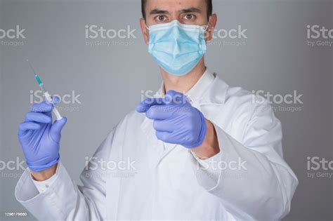 흰색 코트와 파란색 마스크의 의사가 회색 배경에 코로나 바이러스 백신 주사기를 손에 들고 40 44세에 대한 스톡 사진 및 기타