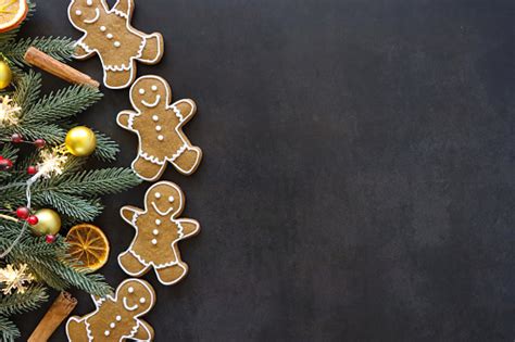 수제 진저 브레드 남자 비스킷 은 흰색 왕실 아이싱 가문비 나무 바늘 금 장식 빨간 베르0리 계피 스틱과 말린 감귤류 오렌지 조각 조명 요정 조명 검은 배경 높은 전망 복사