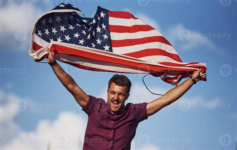 Patriotic Happy Man Waving American Flag Against Cloudy Blue Sky
