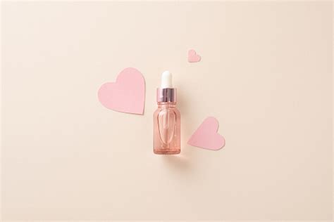 빈 공간이 있는 파스텔 베이지색 배경에 작은 분홍색 하트가 있는 세럼 병의 평면도를 보여주는 컨셉으로 고급스러운 스킨 케어를