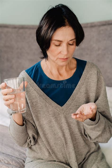 White Mature Woman Taking Medicine While Sitting On Bed Stock Image