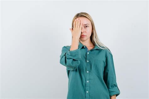 녹색 블라우스에 손으로 얼굴의 일부를 덮고 심각한 찾고 금발 소녀 무료 사진