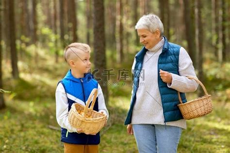 采摘季节、休闲和人的概念 快乐微笑的祖母和孙子在森林里提着篮子和蘑菇。高清摄影大图 千库网