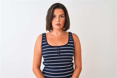 고립 된 흰색 배경 위에 서있는 파란색 줄무늬 티셔츠를 입은 젊은 아름다운 여성은 얼굴에 심각한 표정으로 편안합니다 카메라를 보는 간단하고 자연스러운 T 셔츠에 대한 스톡