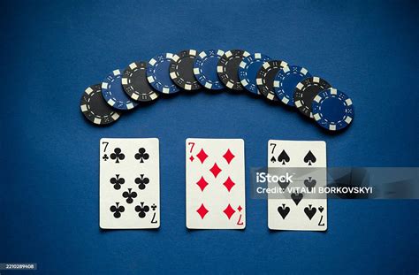 포커 칩과 카드 놀이가 파란색 테이블에 가지런히 정리되어 있습니다 이 카드에는 3개의 7이 표시되어 있으며 이는 카드 게임 설정에서 잠재적인 승리 핸드를 나타냅니다 7에