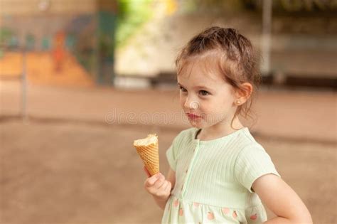 Cheerful Fair Haired Girl In A Dress Eats An Ice Cream Cone Outdoors