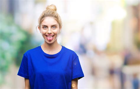 젊은 아름 다운 금발 및 파란 눈 여자를 입고 파란 T셔츠에 고립 된 배경에서 혀를 내밀고 재미 있는 표정으로 행복 감정 개념입니다 T 셔츠에 대한 스톡 사진 및 기타