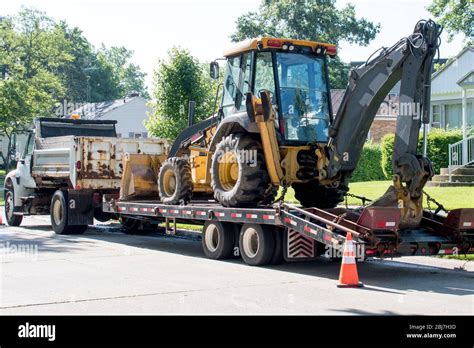 A Dump Truck Delivers A Front End Loader Back Hoe On A Trailer To A City Street So That Road