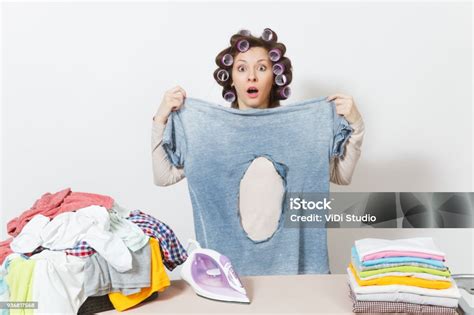 미친 주부 Curlers 들고 가벼운 옷에 머리에 구운 셔츠 다림 질 보드에 서 서 쇠에 의해 만든 구멍 충격된 재미 흰색 배경에 고립 된 여자입니다 광고에 대 한 공간을