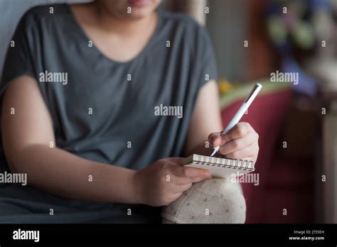 Left Handed Woman Writing Some Idea On Small Notepad While Sitting On Chair In House Freelance